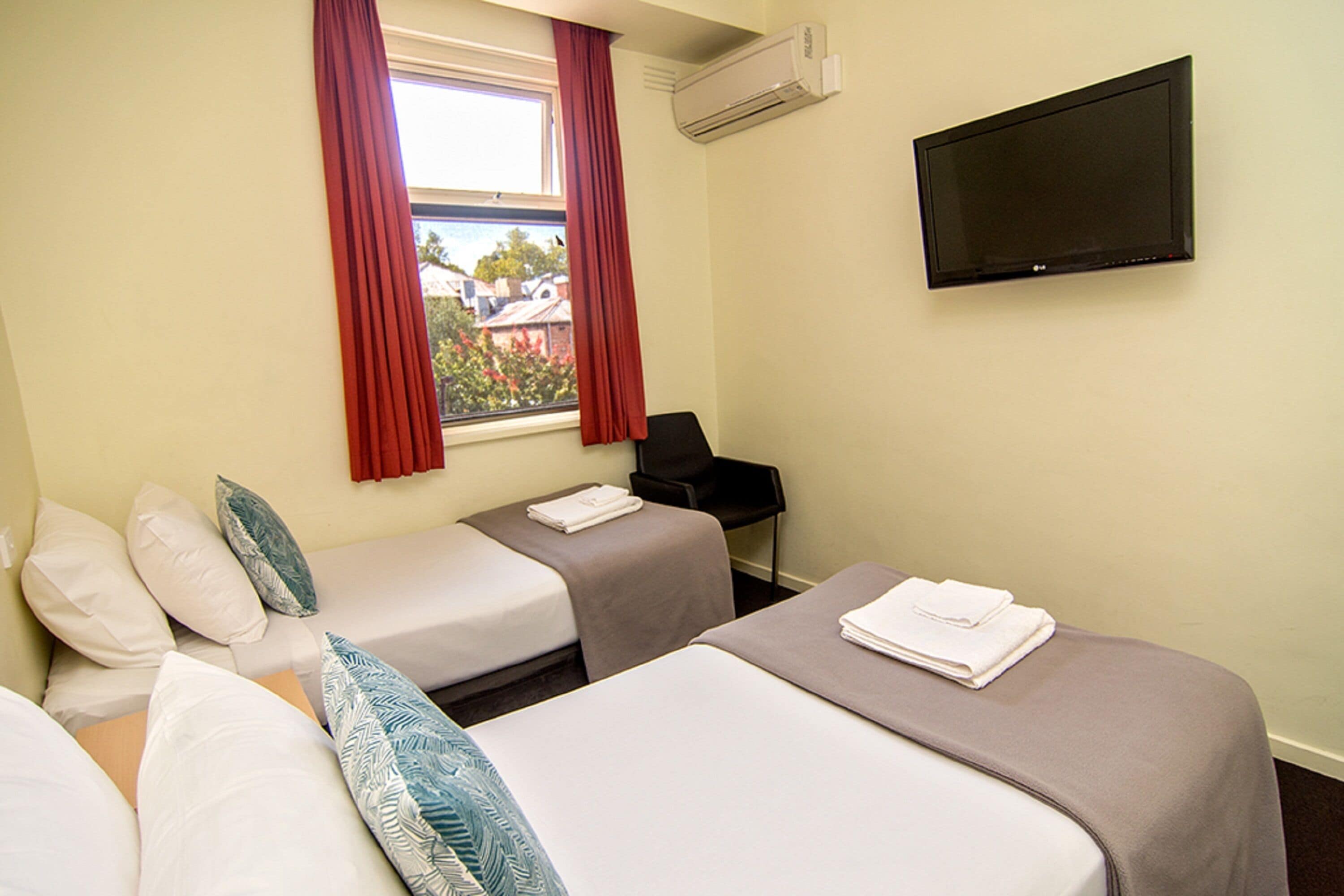 Quarto de hotel com duas camas, uma televisão presa na parede e uma janela com cortinas vermelhas.