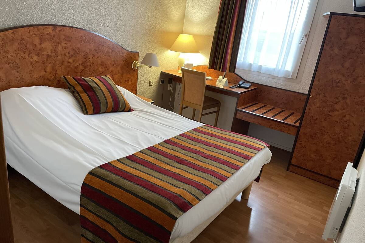 Quarto de hotel com cama, escrivaninha, cadeira e abajur.