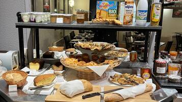 Um buffet de café da manhã com diversos pães, bolos e bebidas.