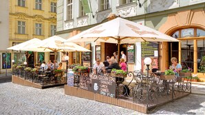 Um café ao ar livre com mesas e guarda-s óis, rodeado por edifícios históricos.
