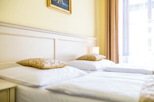 Quarto de hotel com duas camas, cabeceira, mesa de cabeceira e janela com cortinas.