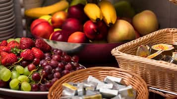 Uma mesa com diversas frutas, incluindo morangos, uvas e maçãs, e uma cesta de vime com chocolates.