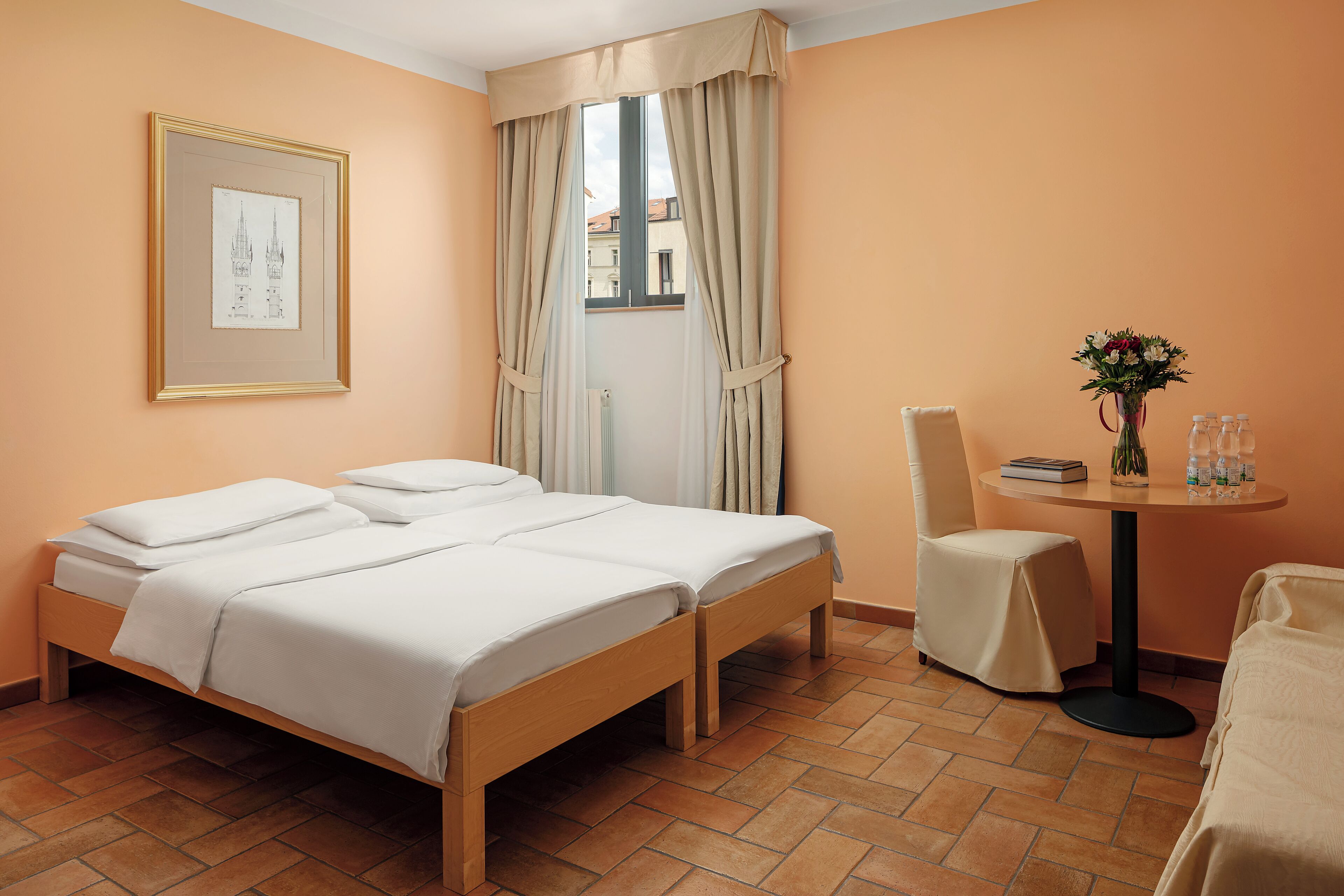 Quarto de hotel com cama, uma cadeira, uma mesinha e um quadro na parede.