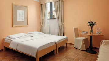Quarto de hotel com cama, uma cadeira, uma mesinha e um quadro na parede.