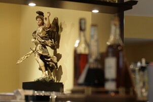 Uma estátua em um pedestal em um espaço bem iluminado, com um fundo desfocado de garrafas.
