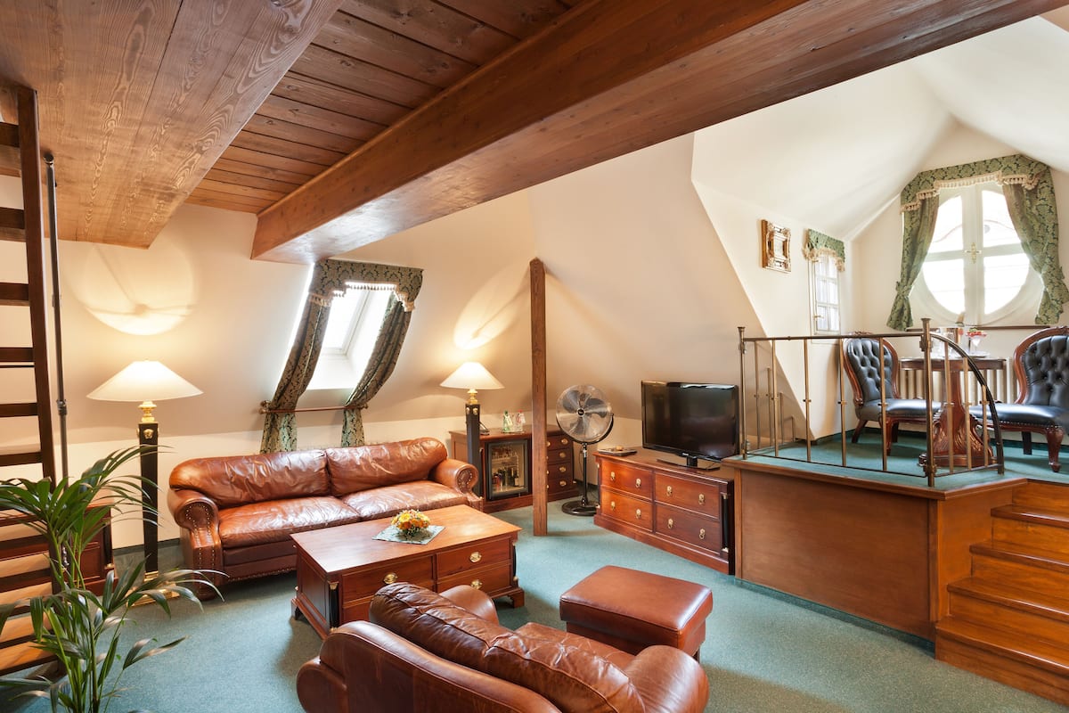 Uma sala de estar aconchegante no estilo loft, com teto alto, vigas de madeira, sofá de couro, mesa de centro e televisão.