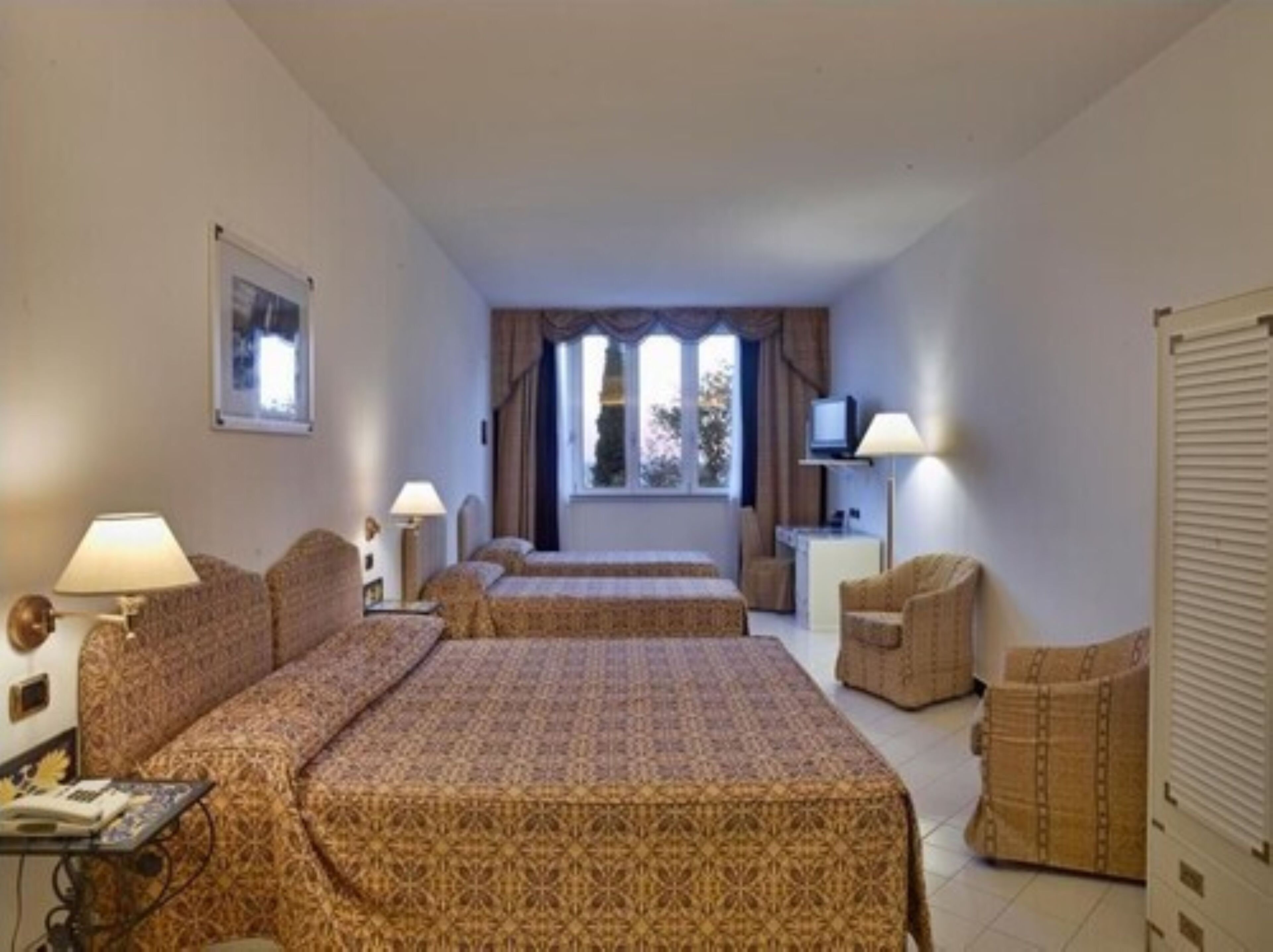 Quarto de hotel com duas camas, uma escrivaninha, uma cadeira, uma televisão e uma janela com cortinas.