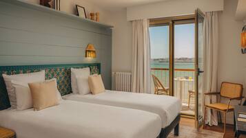 Quarto de hotel com duas camas, varanda e vista, uma pequena mesa e uma cadeira.