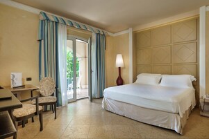 Quarto de hotel com cama, escrivaninha, cadeira, abajur e vista para o exterior.