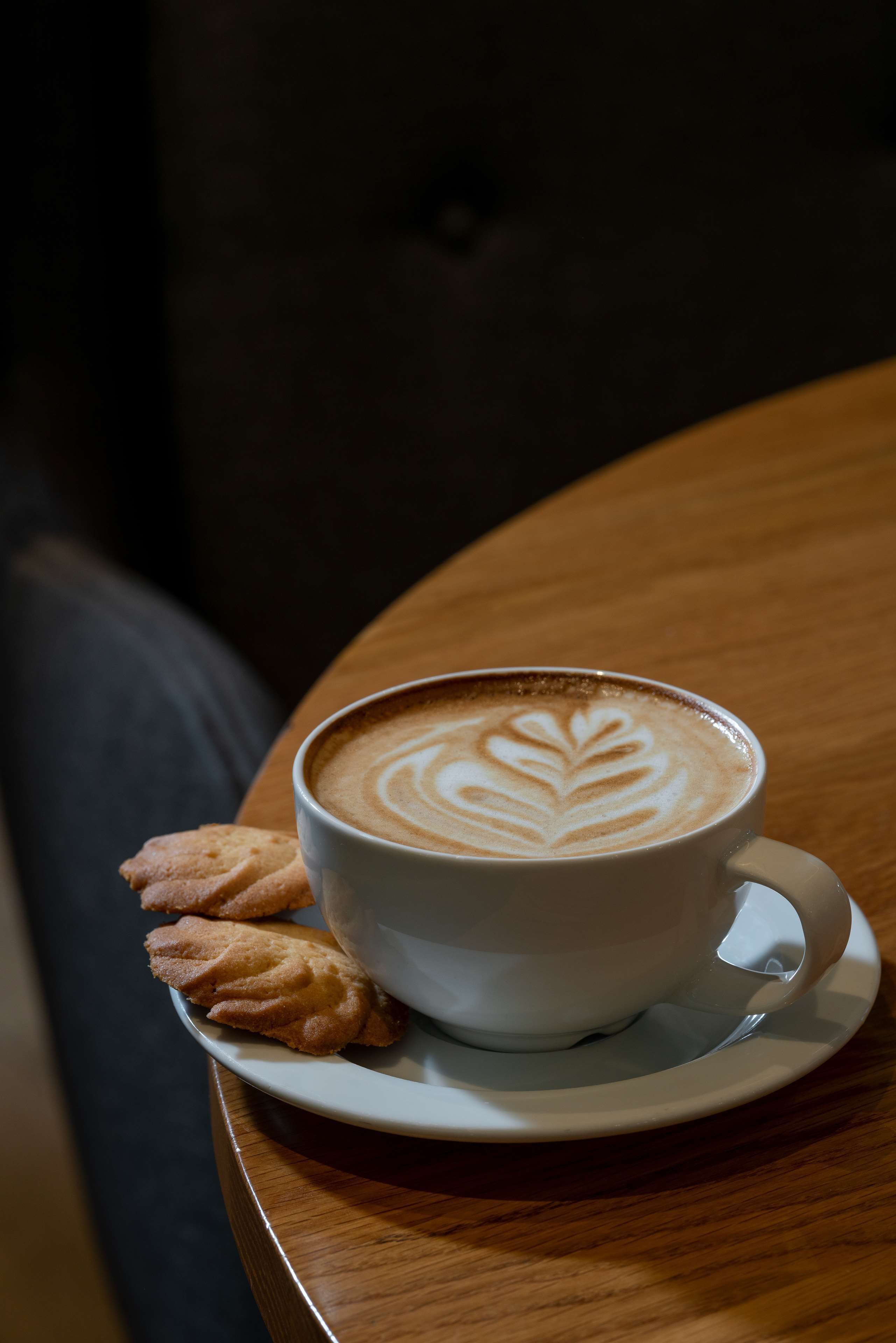 Uma chávena de café com arte de latte num pires, acompanhada por um prato de biscoitos.