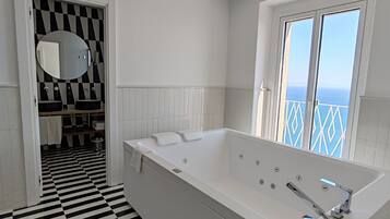 Uma casa de banho moderna com uma banheira grande, um espelho e vista para o mar através de uma janela.