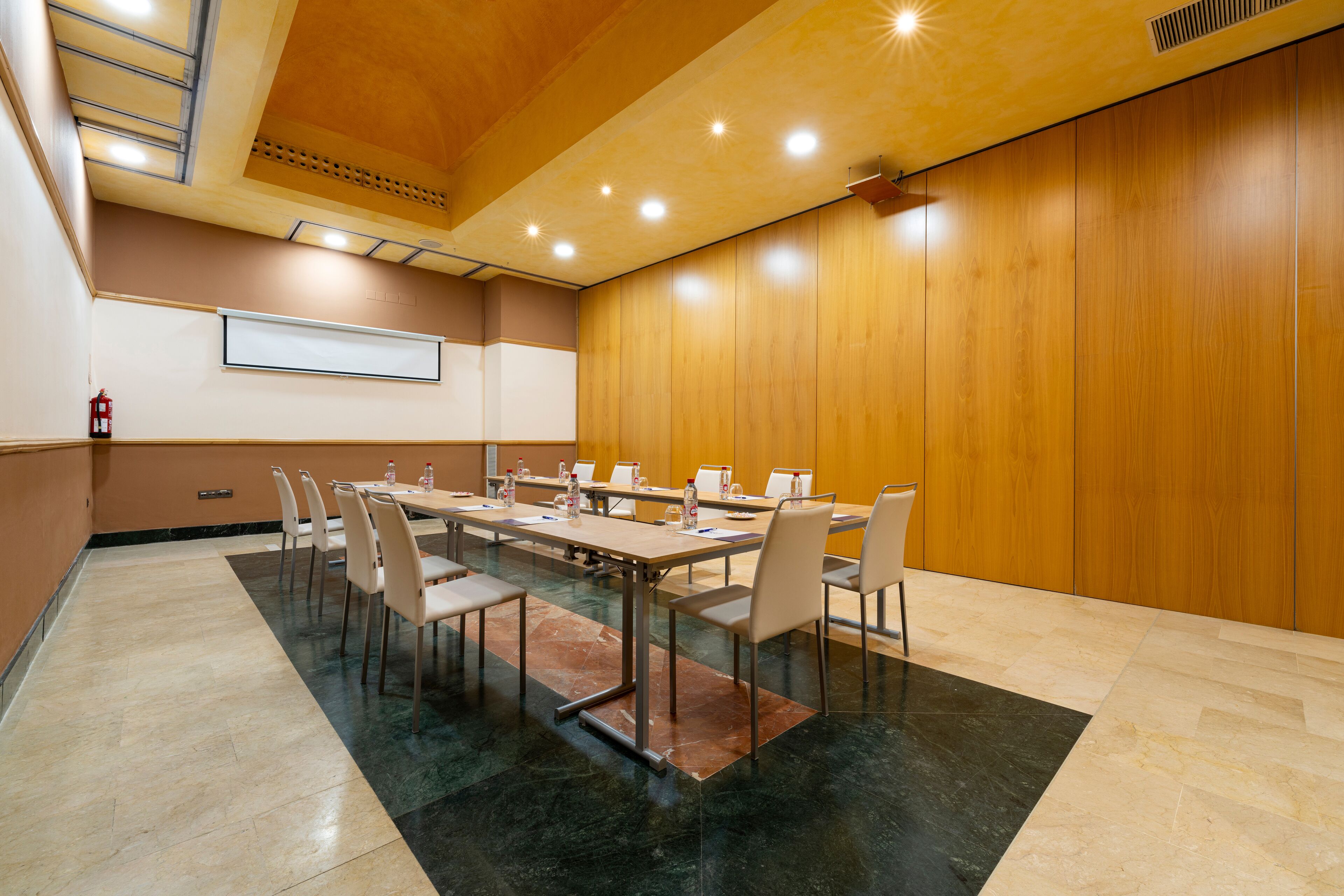Uma sala de conferências com uma mesa comprida, cadeiras, uma tela de projetor e painéis de madeira.