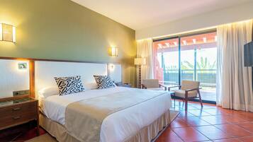 Quarto de hotel com uma cama grande, uma mesinha de cabeceira, uma cadeira e vista para o exterior.