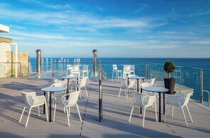 Terraço no telhado com cadeiras e mesas brancas, com vista para o oceano.