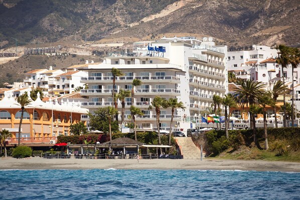 Um hotel à beira-mar com várias varandas, localização na praia e um cenário montanhoso.
