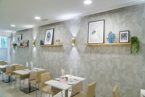 Uma sala de jantar moderna com mesas e cadeiras, obras de arte emolduradas nas prateleiras e um painel de parede estampado.