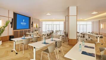 Sala de conferências com várias mesas e cadeiras, uma tela grande exibindo 'HIPOTELS Hotels & Resorts' e piso de madeira.