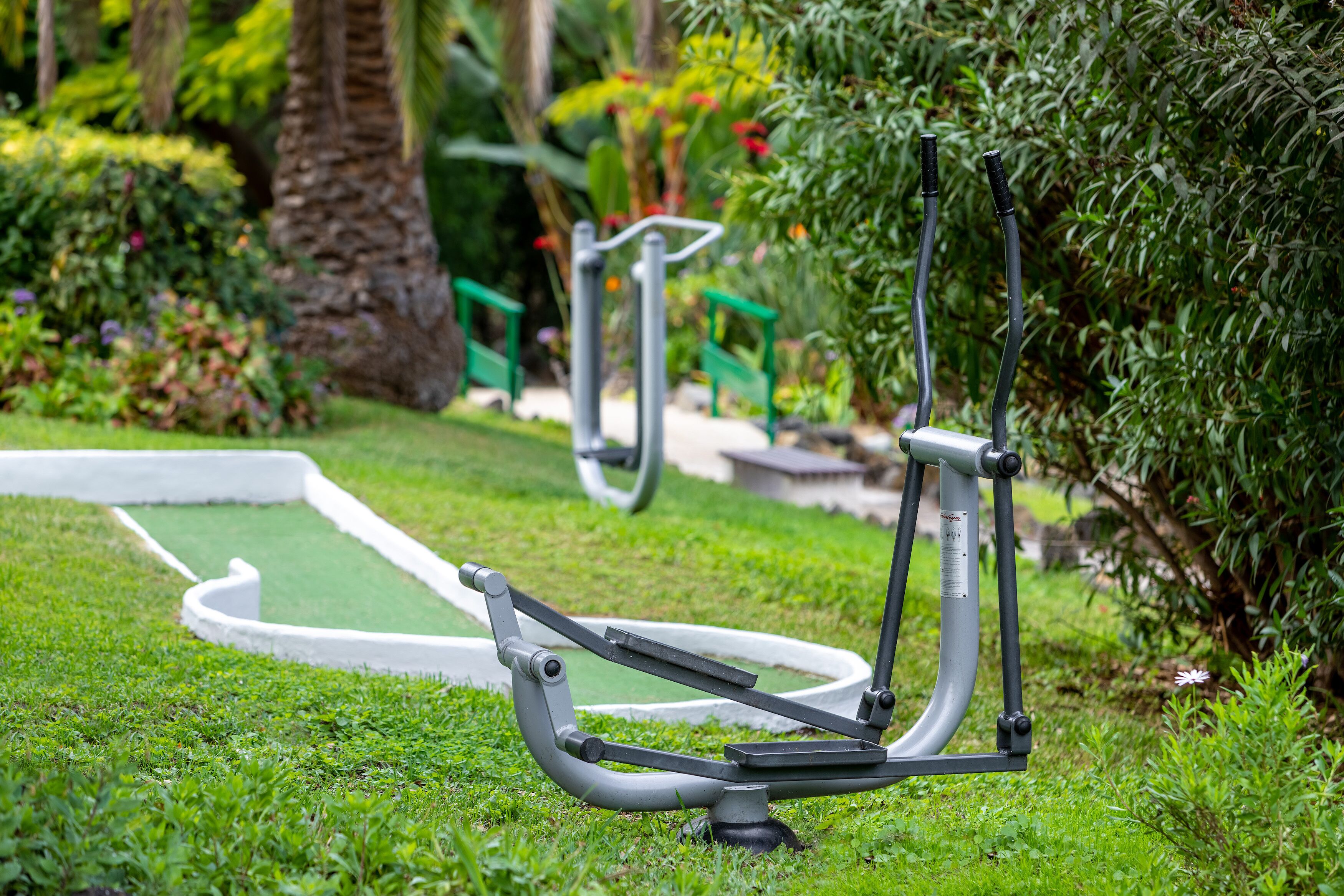 Aparelho de ginástica ao ar livre em um jardim com vegetação e uma pequena piscina.