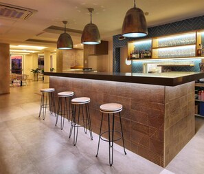 Uma área de bar com parede estampada, três banquetas e luminárias pendentes.