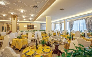 Uma sala de jantar formal com várias mesas postas para refeição, com toalhas de mesa amarelas e cadeiras brancas.