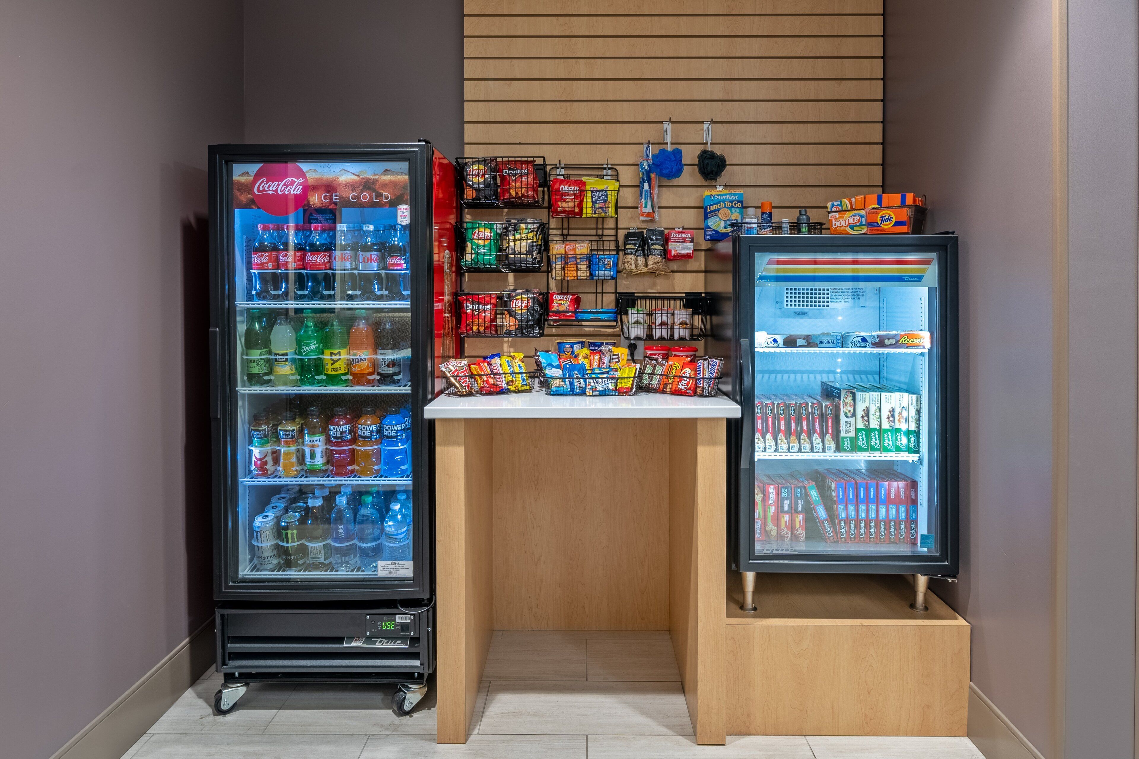 Uma área de distribuição automática com Coca-Cola e outras bebidas, lanches e um refrigerador.