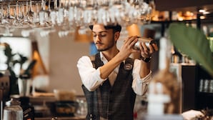 Um bartender prepara uma bebida atrás do balcão, com copos e garrafas.
