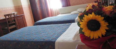 Quarto de hotel com duas camas, uma escrivaninha, uma cadeira, televisão e um buquê de girassóis.