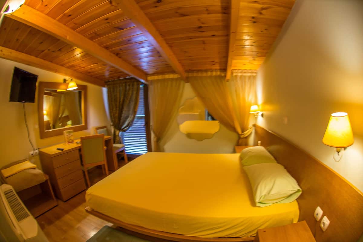 Um quarto com teto de madeira, uma cama com colcha amarela, uma escrivaninha com cadeira, um espelho e uma luminária fixada na parede.