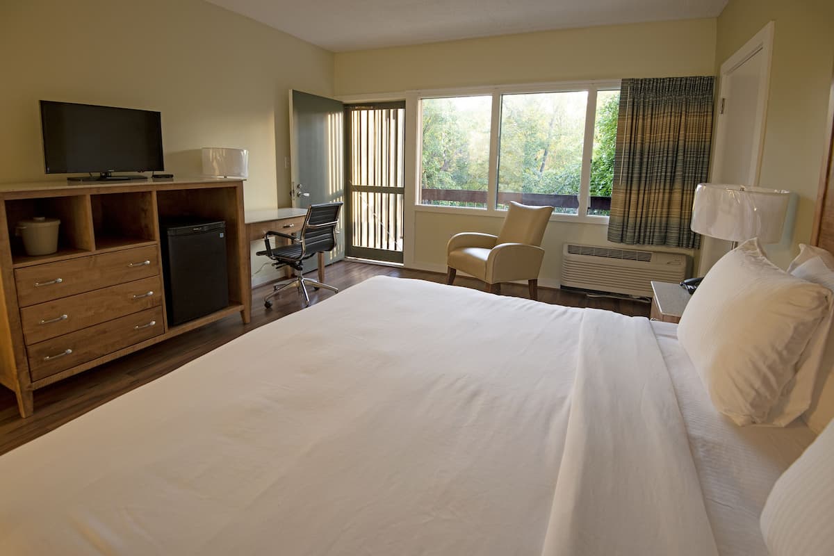 Quarto de hotel com uma cama grande, uma escrivaninha com cadeira, televisão, mini-geladeira e janela com cortinas.