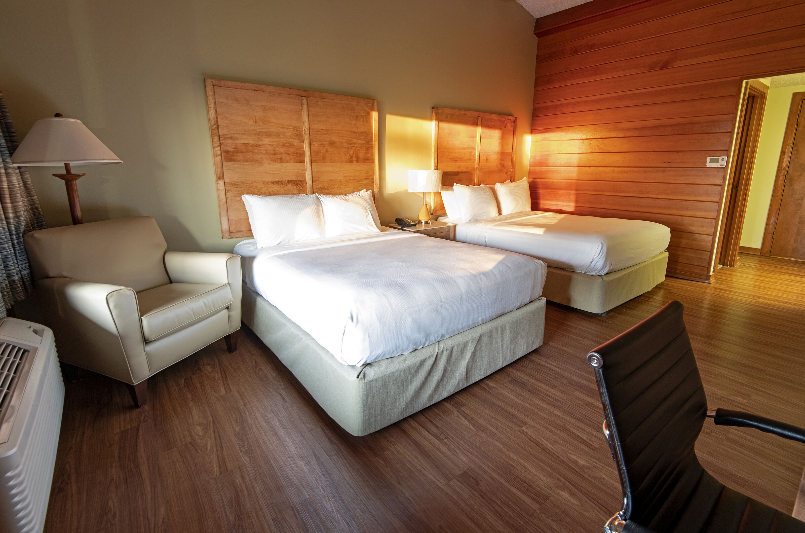 Quarto de hotel com duas camas, uma cadeira, um abajur e um aquecedor.