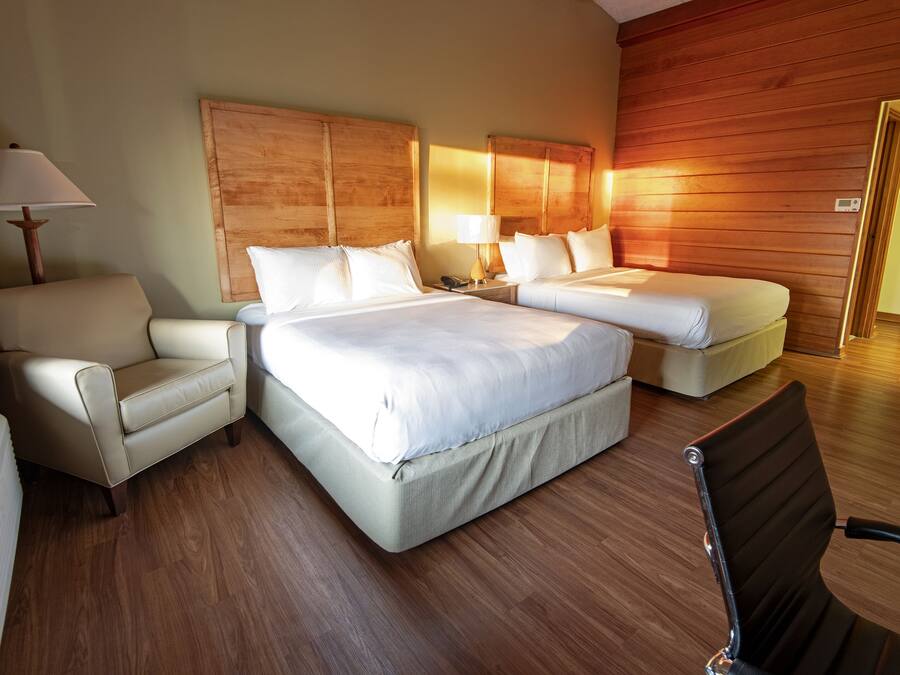 Quarto de hotel com duas camas, uma cadeira, um abajur e um aquecedor.