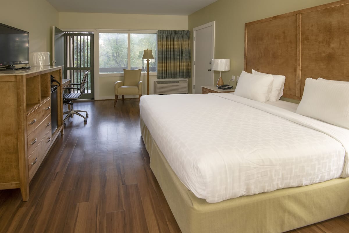 Quarto de hotel com uma cama grande, uma escrivaninha com cadeira, televisão e janela com cortinas.
