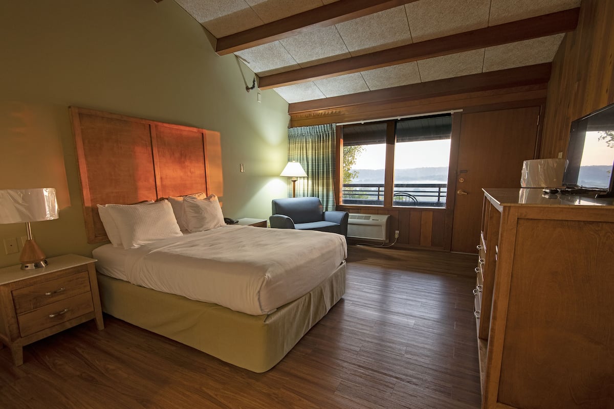Quarto de hotel com cama grande, escrivaninha, cadeira, TV e vista para o exterior.
