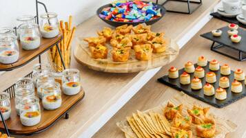 Mesa de buffet com diversos alimentos, incluindo sobremesas, lanches e aperitivos.