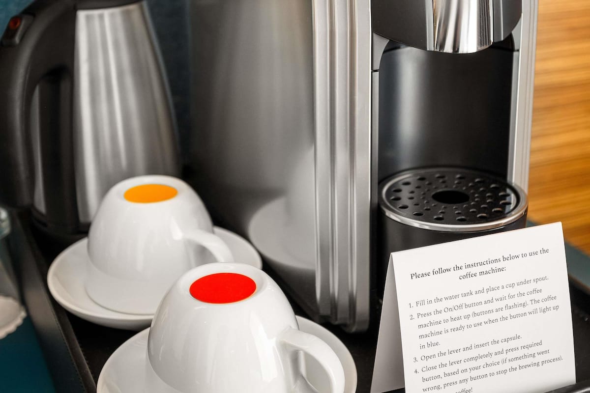 Máquina de café com instruções, duas chávenas com tampas vermelhas e um bule.