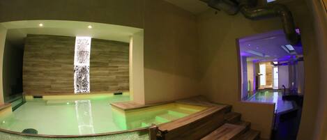 Uma área de spa com uma grande banheira de hidromassagem, degraus de madeira e uma parede com painel decorativo.