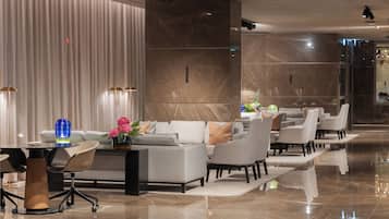 Um lobby de hotel moderno com um sofá, cadeiras, uma mesa de jantar e um vaso decorativo.