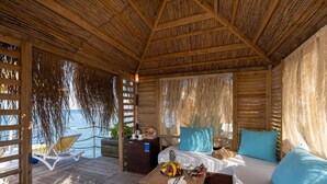 Um deck de madeira com uma cama, uma mesa com frutas e vista para o mar.