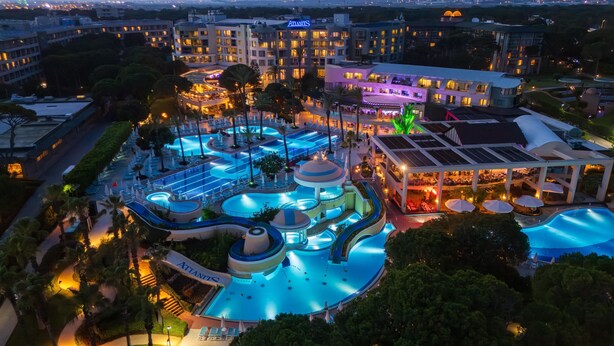 Um resort com várias piscinas, um edifício grande com a inscrição 'Atlantis' e uma área coberta com guarda-sóis.