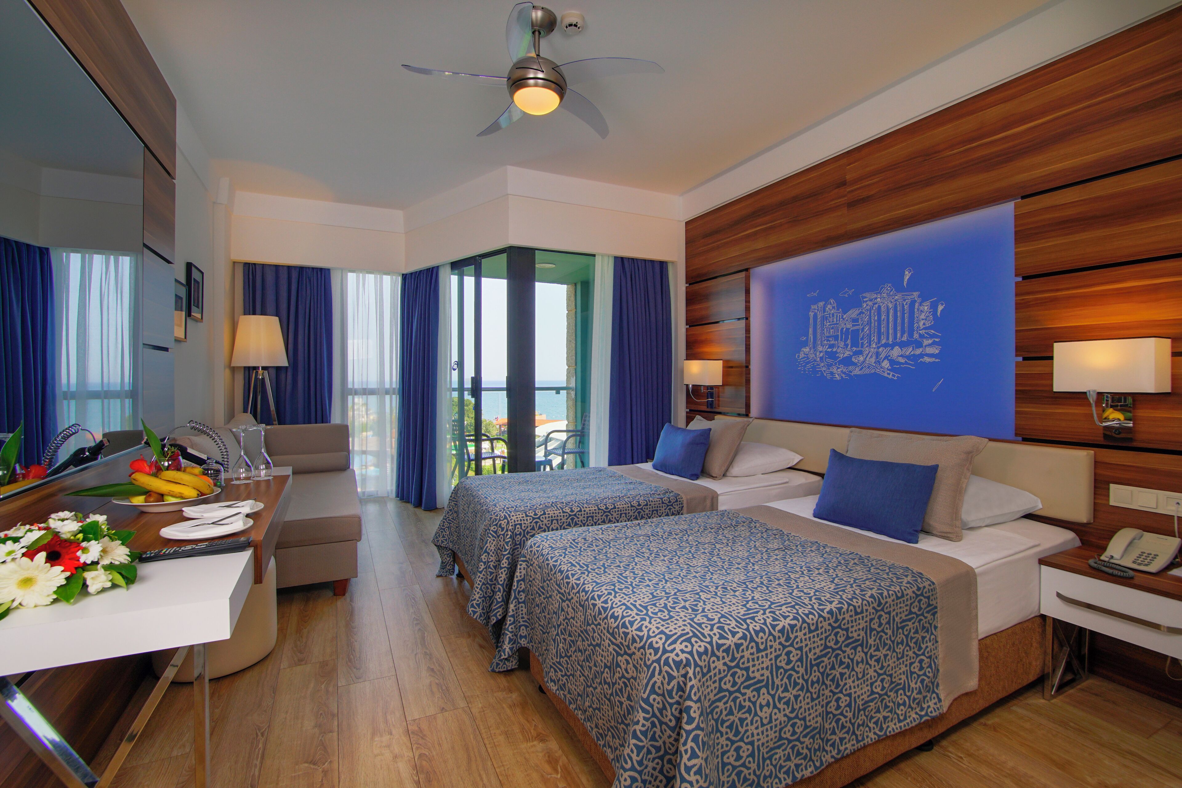 Quarto de hotel com duas camas, uma mesa com uma cesta de frutas, um telefone e vista para o exterior.