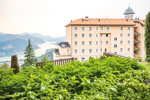 Edifício de vários andares com varanda, rodeado por vegetação exuberante e com vista para um corpo de água.