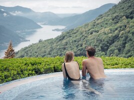 Um casal sentado em uma piscina com vista para um lago e montanhas.