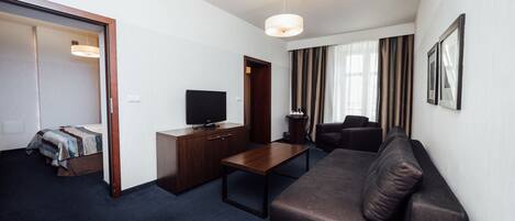 Quarto de hotel com sofá, televisão, escrivaninha e guarda-roupa.