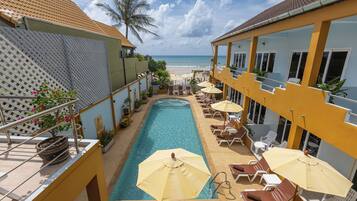 Uma área de piscina com espreguiçadeiras e guarda-sóis, vista para a praia e um edifício com telhado em azulejos.