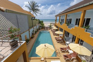 Uma área de piscina com espreguiçadeiras e guarda-sóis, vista para a praia e um edifício com telhado em azulejos.