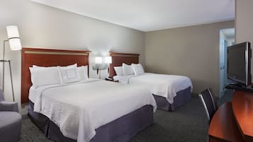 Quarto de hotel com duas camas, uma escrivaninha, uma cadeira, uma televisão e uma luminária.