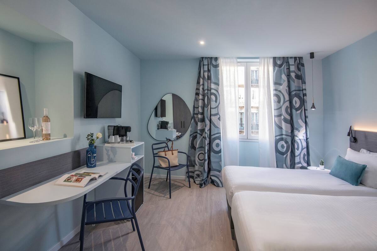 Quarto de hotel moderno com cama, escrivaninha, cadeira, espelho e janela com cortinas.