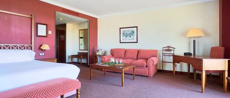 Quarto de hotel com cama, sofá vermelho, escrivaninha de madeira e luminária.