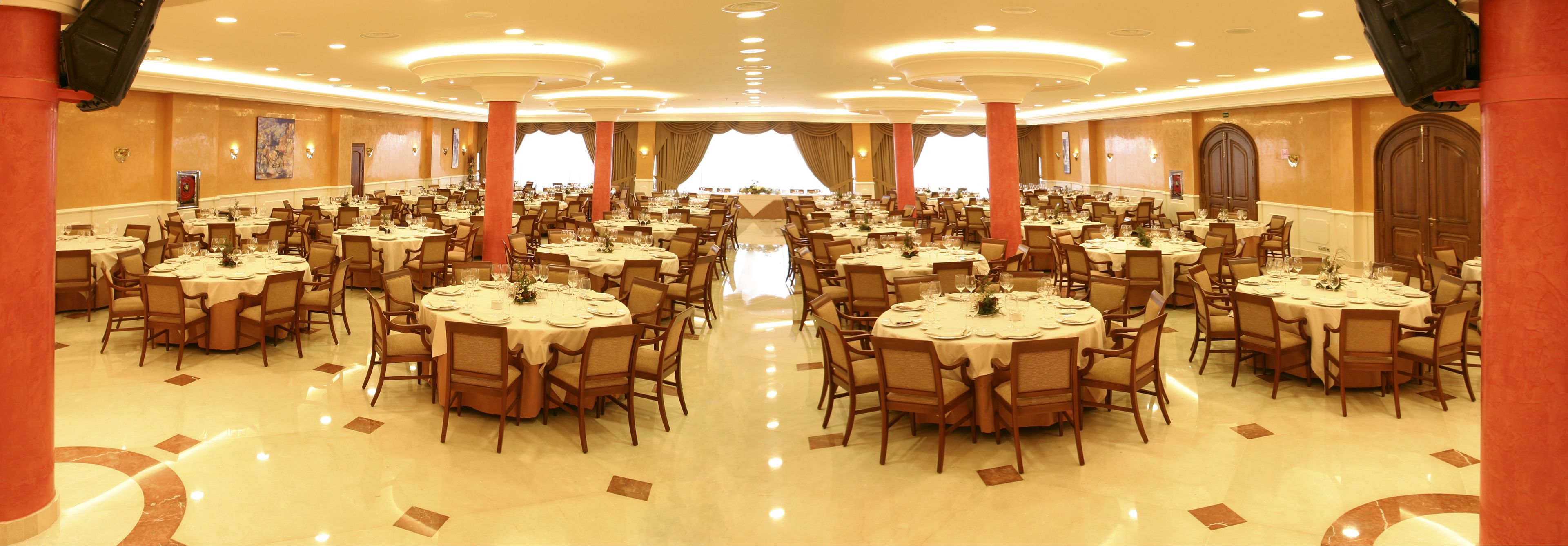 Um amplo salão de banquetes com mesas redondas, cadeiras e piso lustroso.