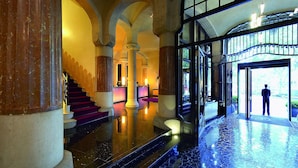 Um amplo hall com pisos de mármore, uma escadaria e um balcão de recepção.